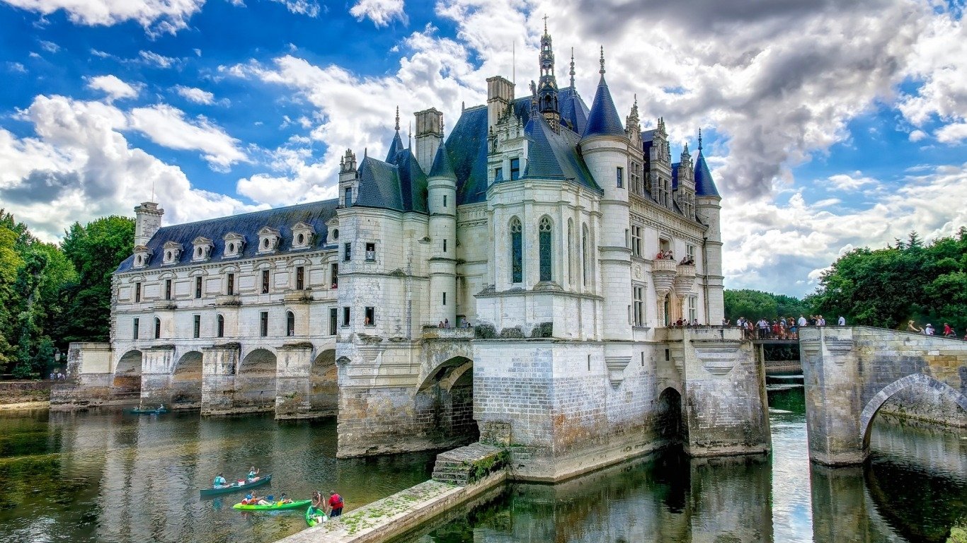 Majestic French Castle Over Tranquil Waters with Boats and Bridge